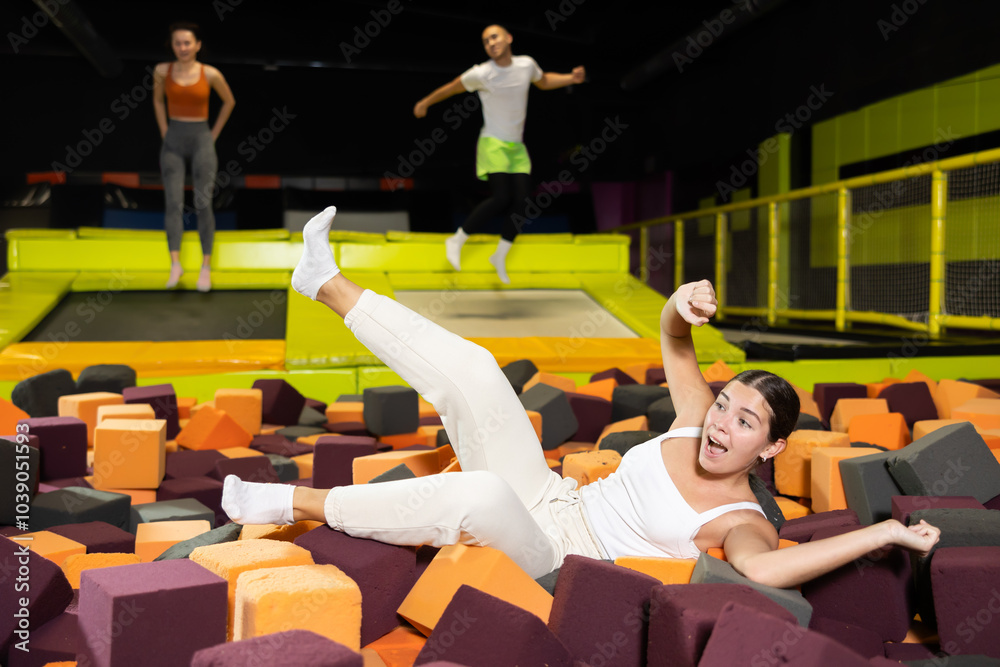 Emotional joyful young girl jumping into foam pit at indoor trampoline ...