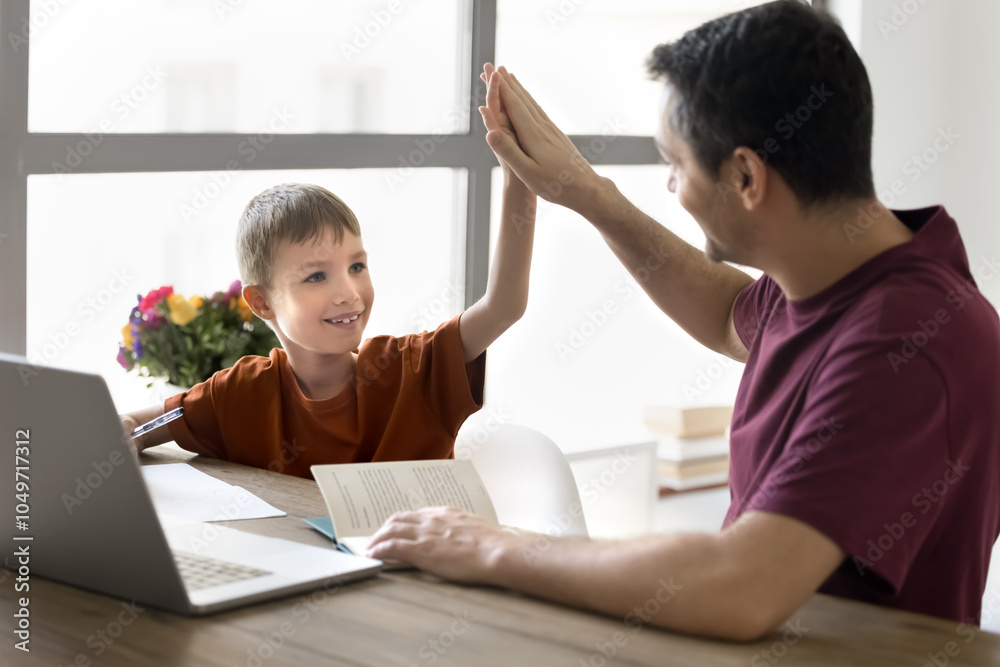 Happy little schoolkid son and proud dad giving high five at home table ...