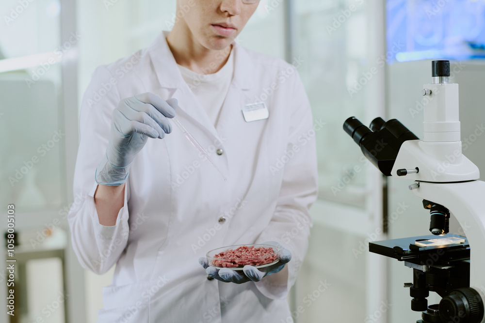 Researcher wearing lab coat and gloves examining lab-grown meat sample ...