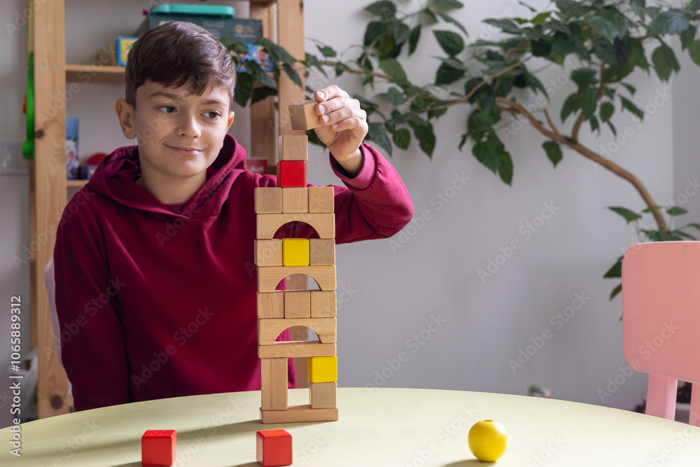 A young boy builds a tower with wooden blocks in a children’s room ...