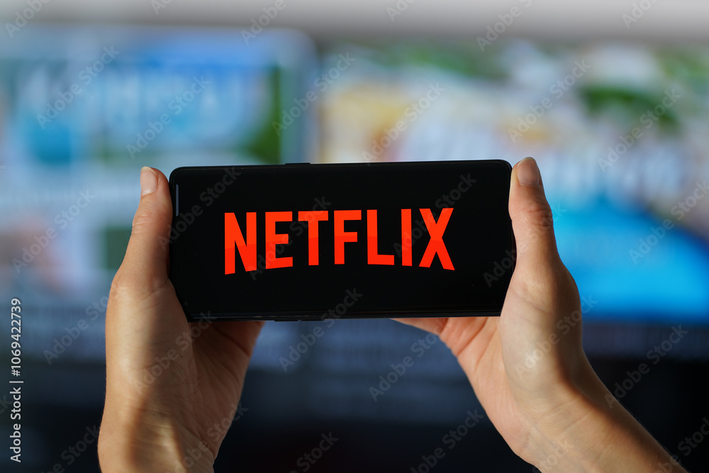 Netflix logo displayed on a screen (cell phone hold by woman with two ...