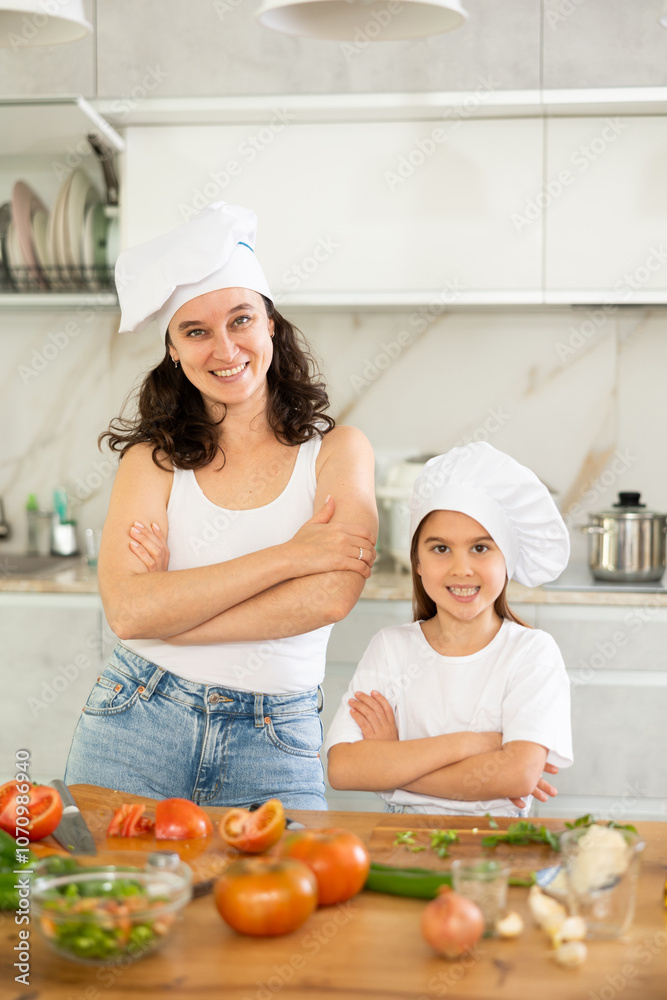 Happy mother and preteen daughter wearing chef hats standing at table ...