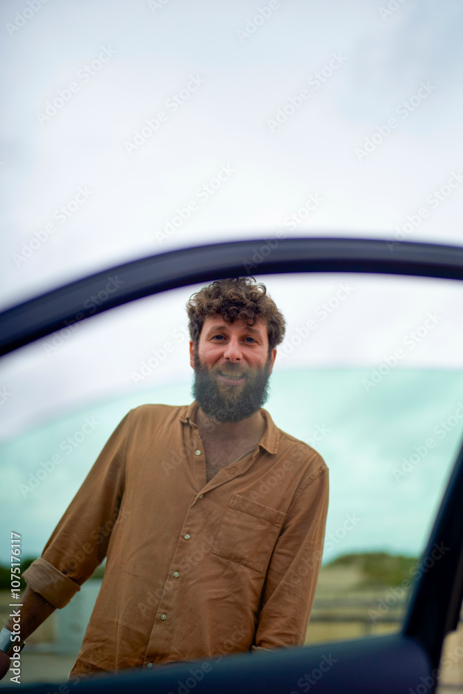Smiling bearded man standing outside viewed through an open car window ...