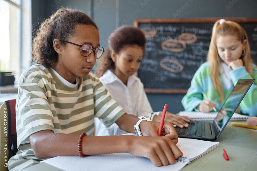 Side view portrait of Black teenage boy wearing glasses and writing in ...
