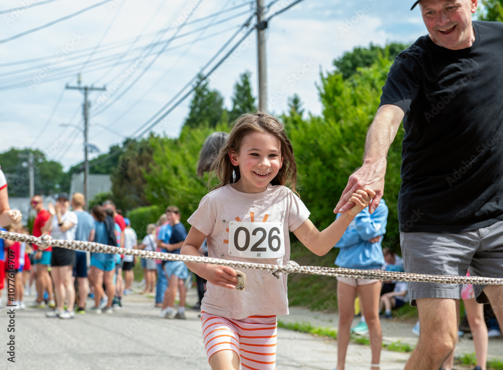 Child and her father run across the finish line at a running race even ...