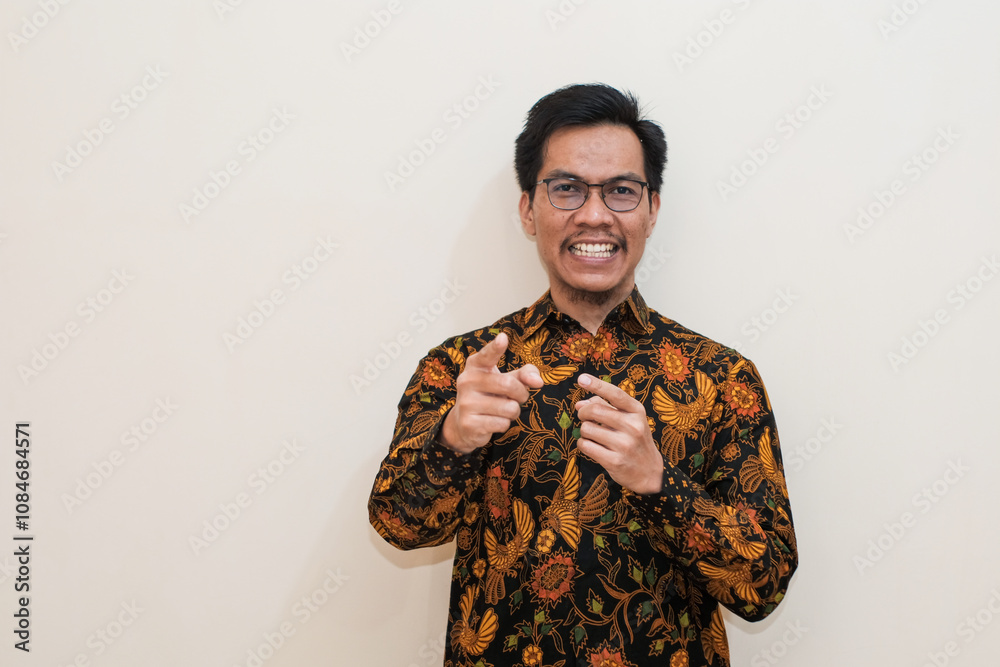 Smiling Southeast Asian man wearing batik shirt and glasses pointing at ...
