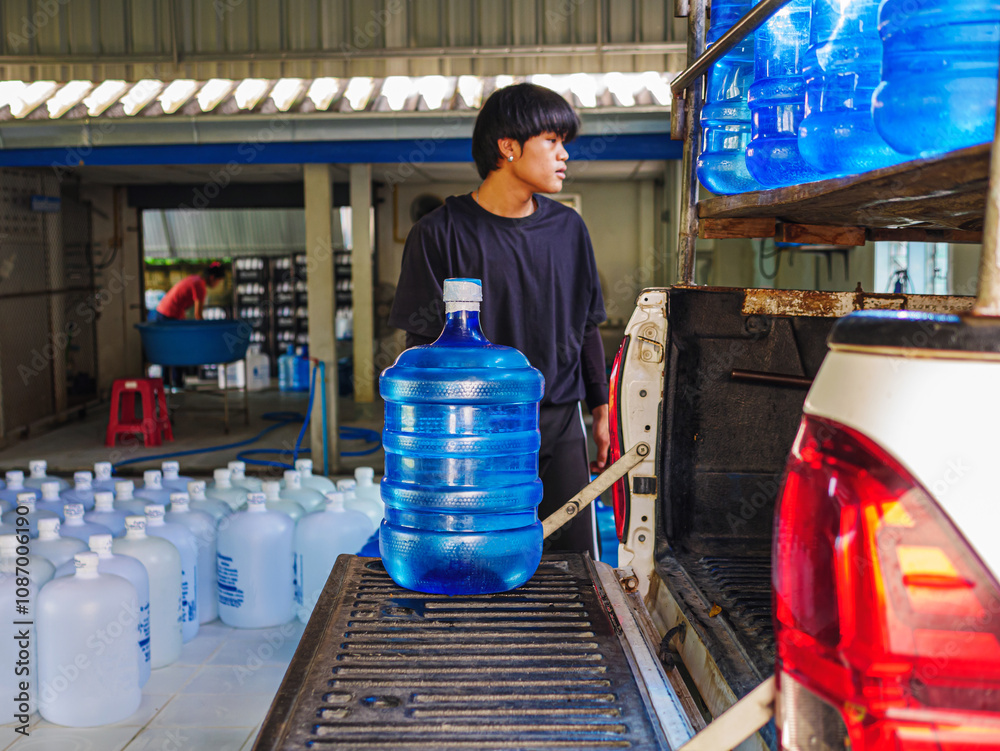 Workers lift blue drinking water gallon into the back of a transport ...