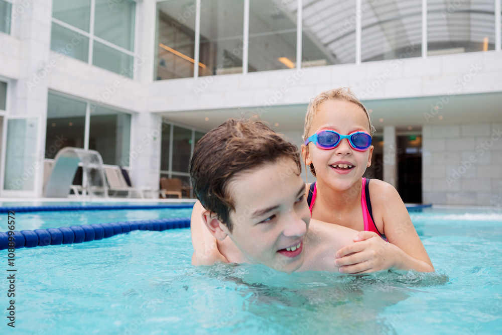 Caucasian siblings playing together as the younger sister rides on her ...