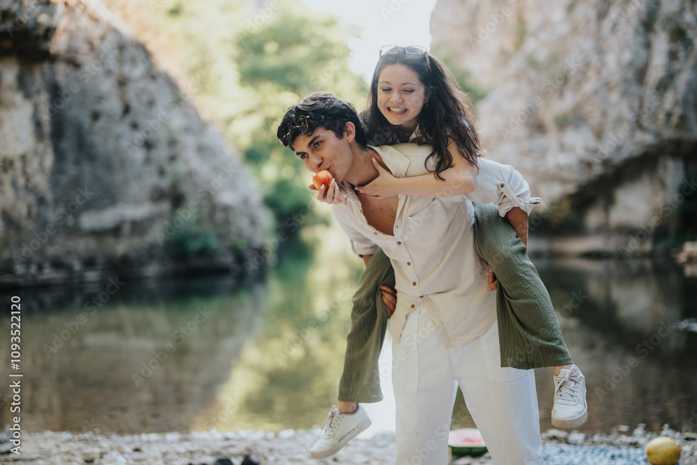 Joyful couple by a river capturing a playful moment. Woman piggybacking ...