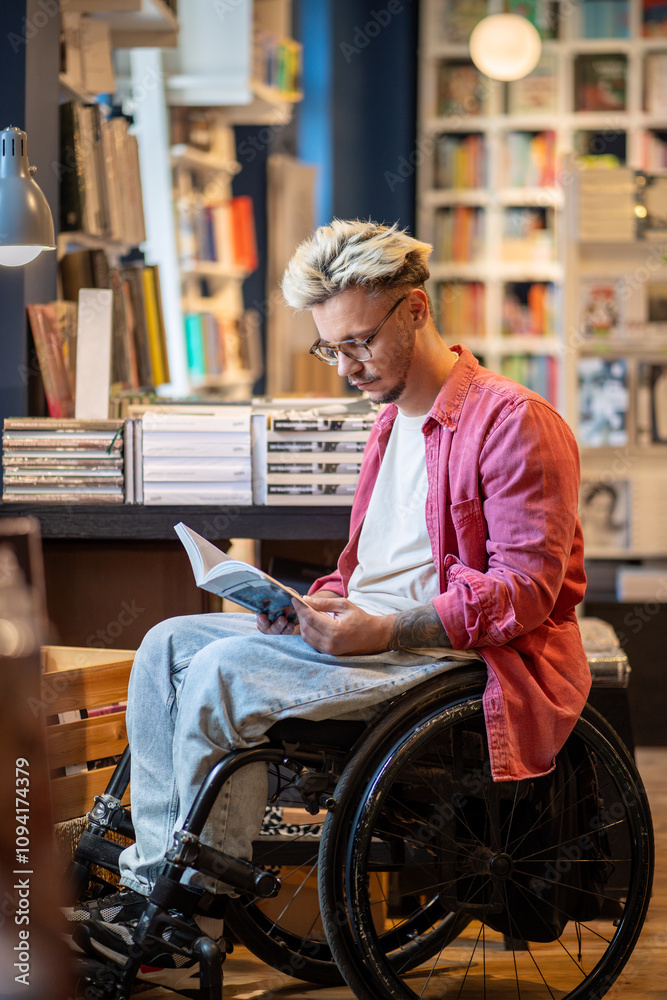 Focused young man with disability reading book in bookstore. Interested ...