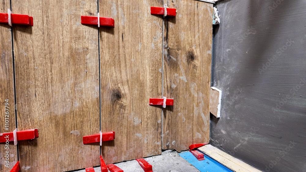 Wood-panel-look tiles being installed on a bathroom wall with red ...