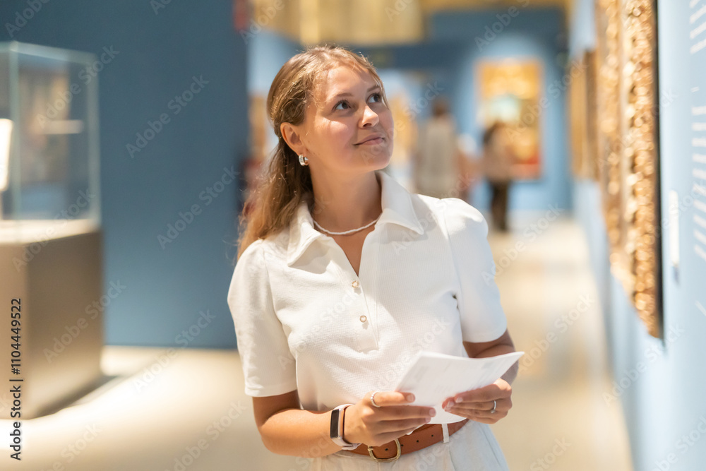 Museum female visitor with paper in hands walk through exhibition halls ...