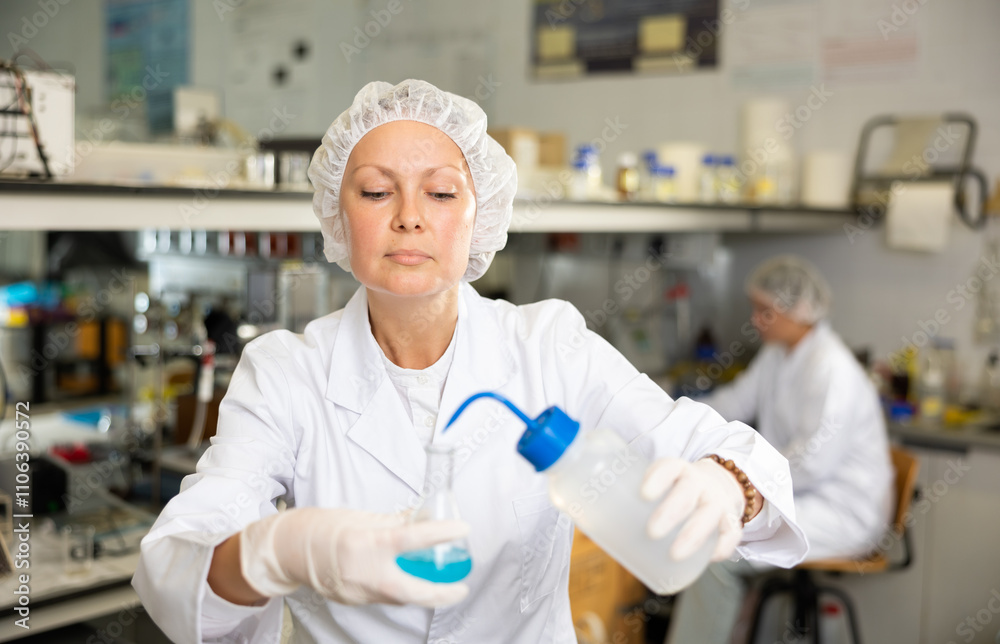 Middle-aged female scientist making research pouring blue reagent into ...