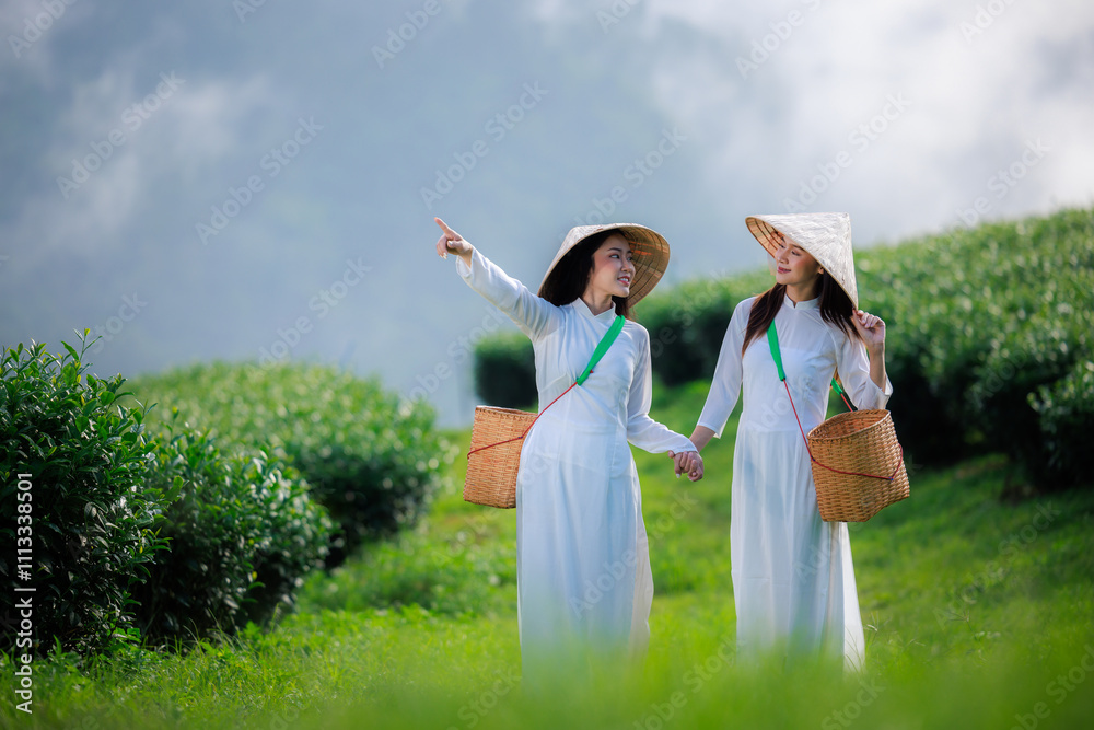 portrait of two young asian woman wearing white vietnamese dress walking and talk about the tea ...