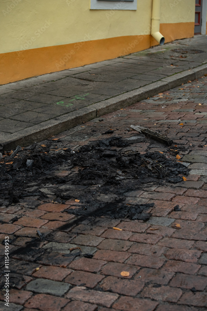 Charred remains on a cobblestone street where a car has burned. The ...