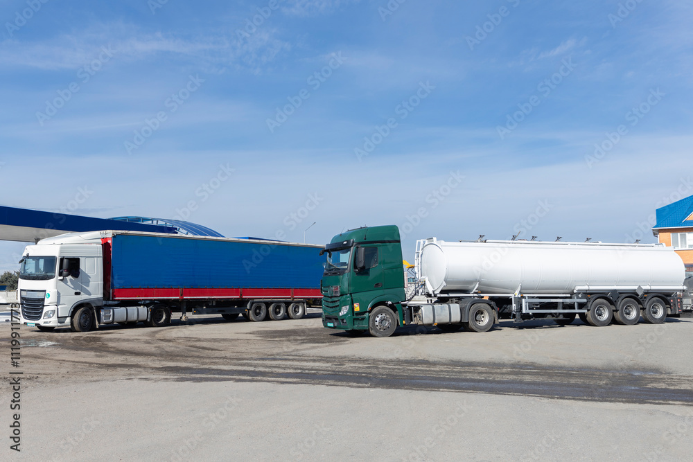 Two long ten-wheel trucks, one with a tank trailer, parked in the ...