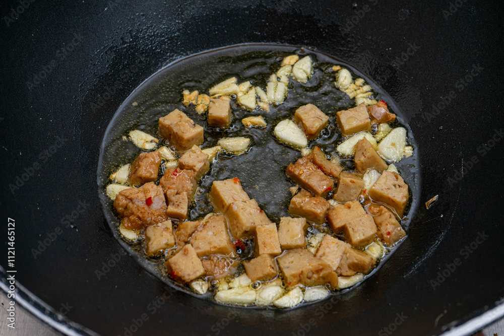 Golden-brown seitan cubes sizzling in a frying pan with garlic and ...