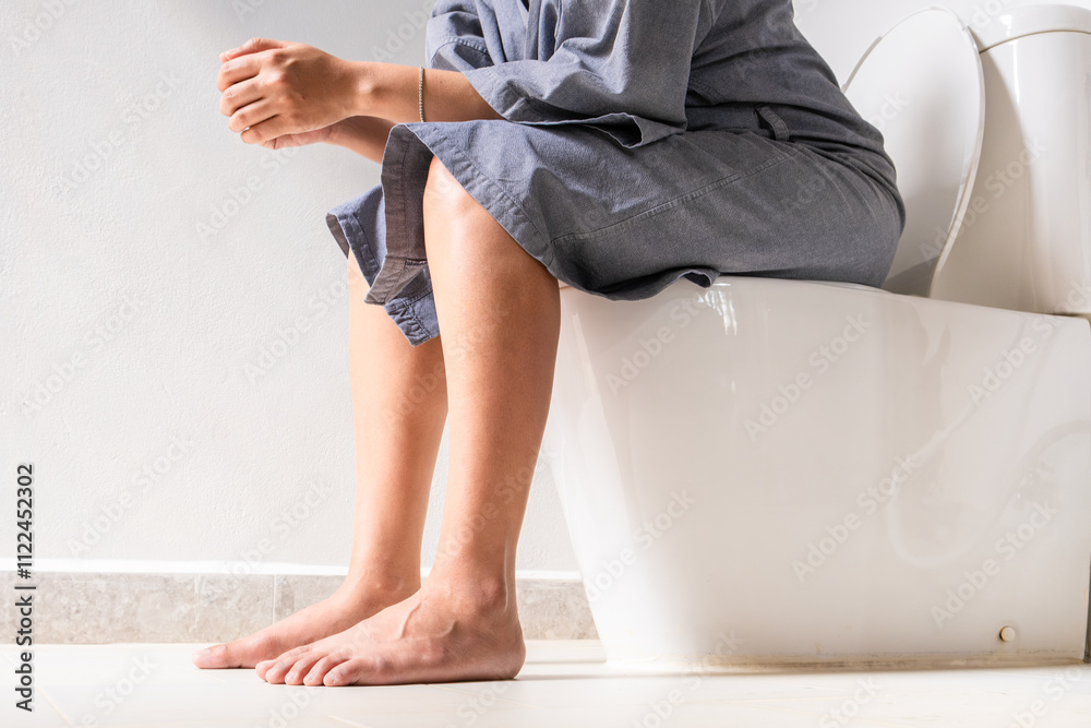 Woman sitting on the toilet bowl in the bathroom. She has stomach ache ...
