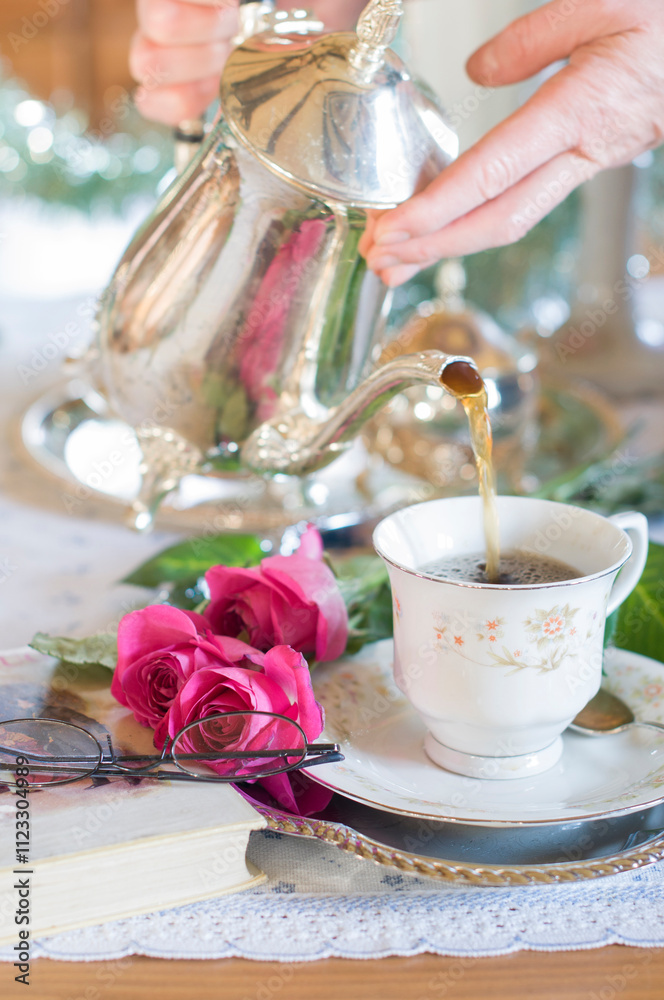English style tea break, female hands pouring tea from a silver teapot ...