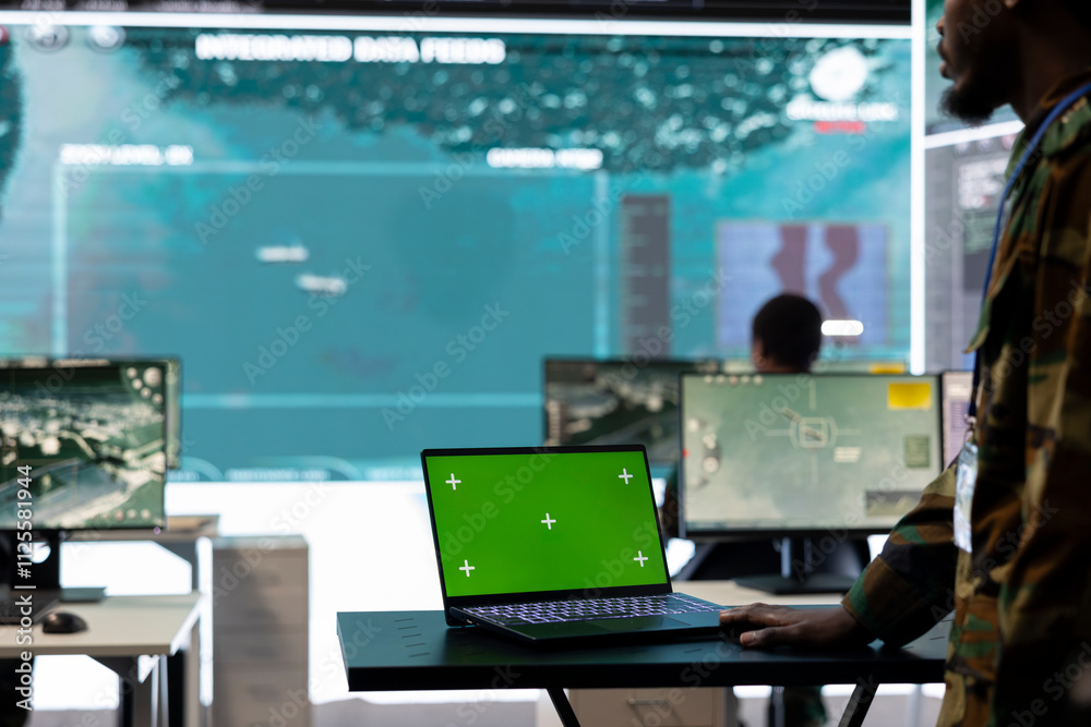Army trooper examines green screen layout on a laptop in control center ...