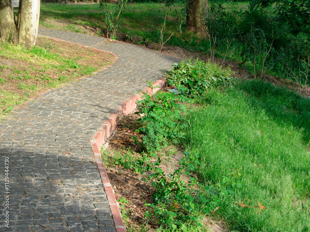 A curved stone pathway with red brick borders, surrounded by lush ...