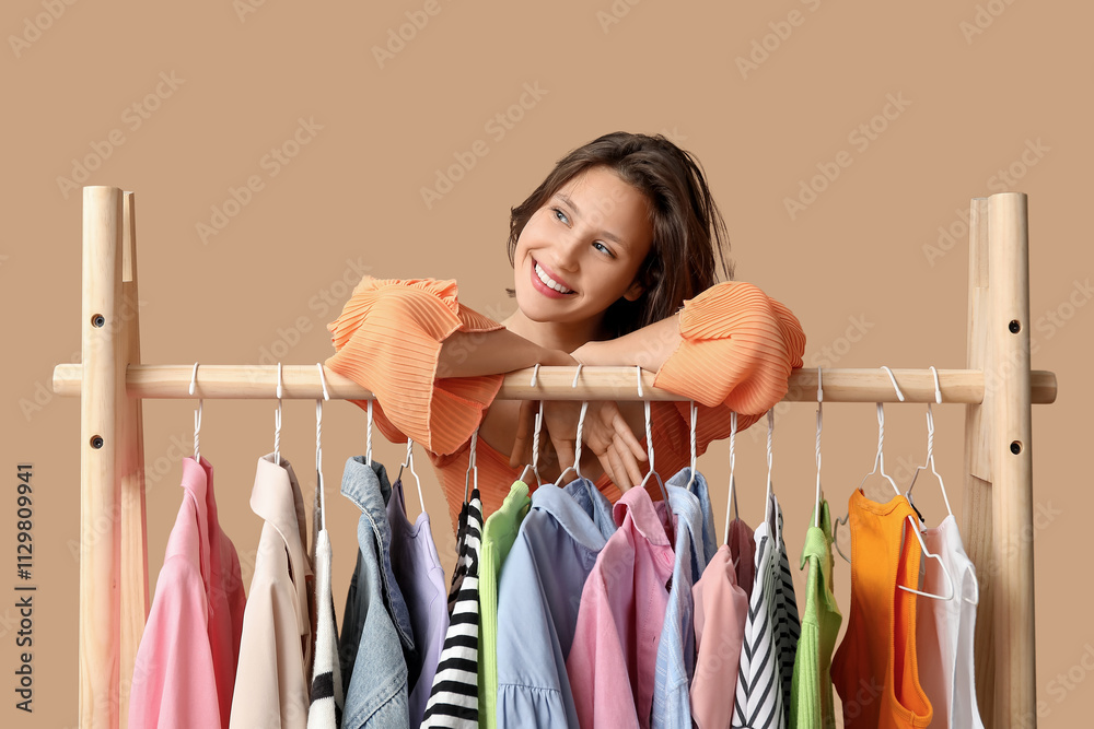 Beautiful young woman near rack with different clothes on beige ...