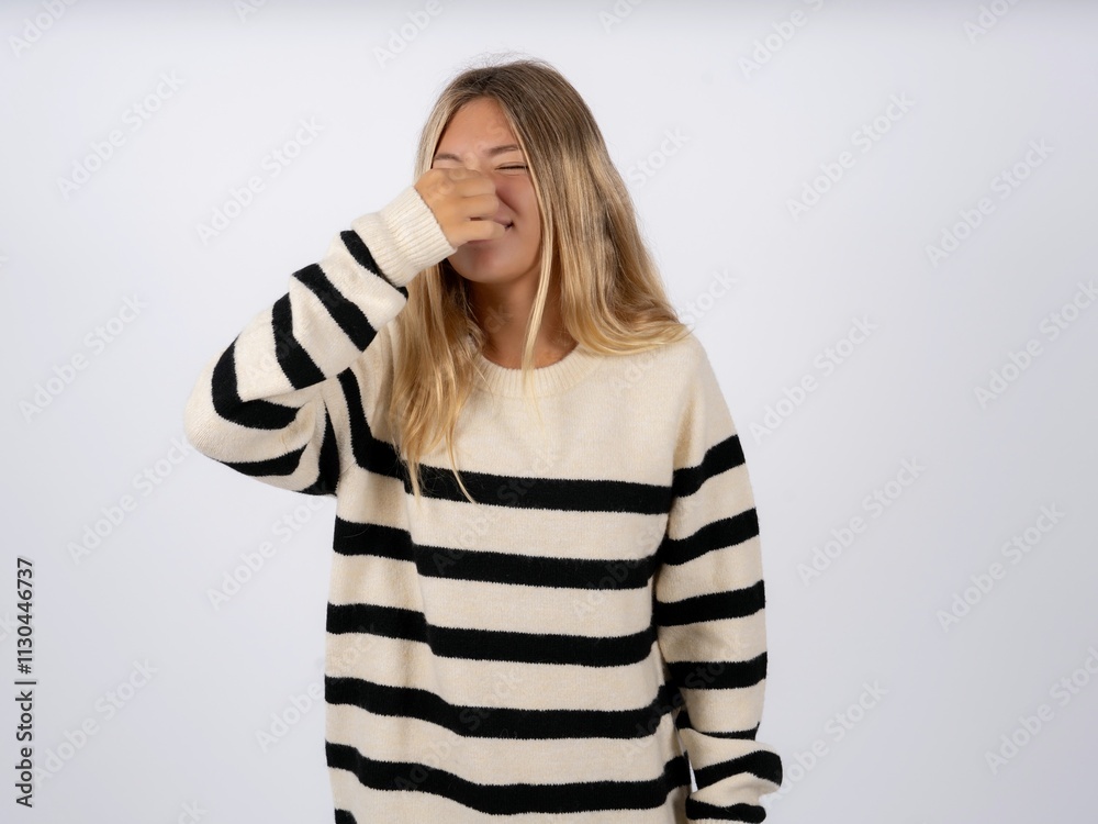 Beautiful teen girl wearing striped sweater smelling something stinky ...