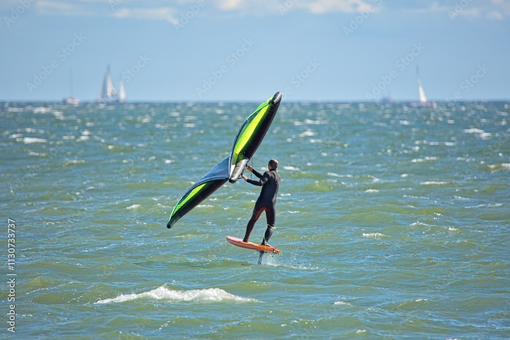 Man is wing foiling using handheld inflatable wing and hydrofoil ...