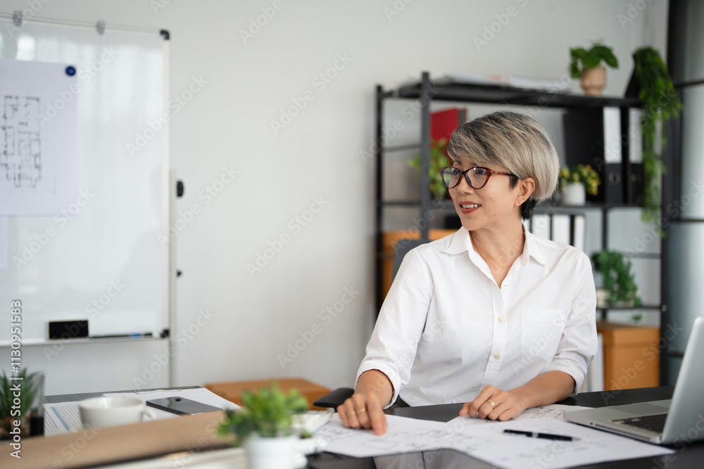 Female architect sitting at her office desk and working with blueprints ...