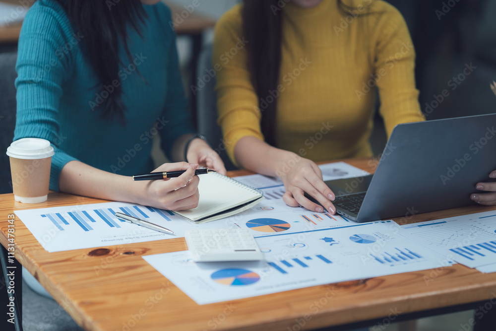 Strategic Collaboration: Two businesswomen analyze financial data on a laptop and notepad ...