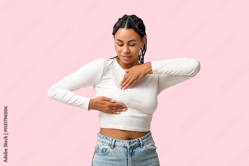 Young African-American woman checking her breast on pink background ...