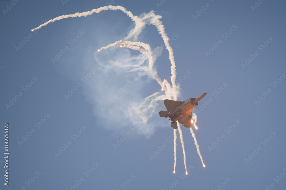 A fighter jet deploys countermeasure flares in the sky, leaving ...