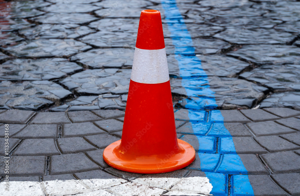 Bright orange road cone stands on the asphalt road, marking caution for ...