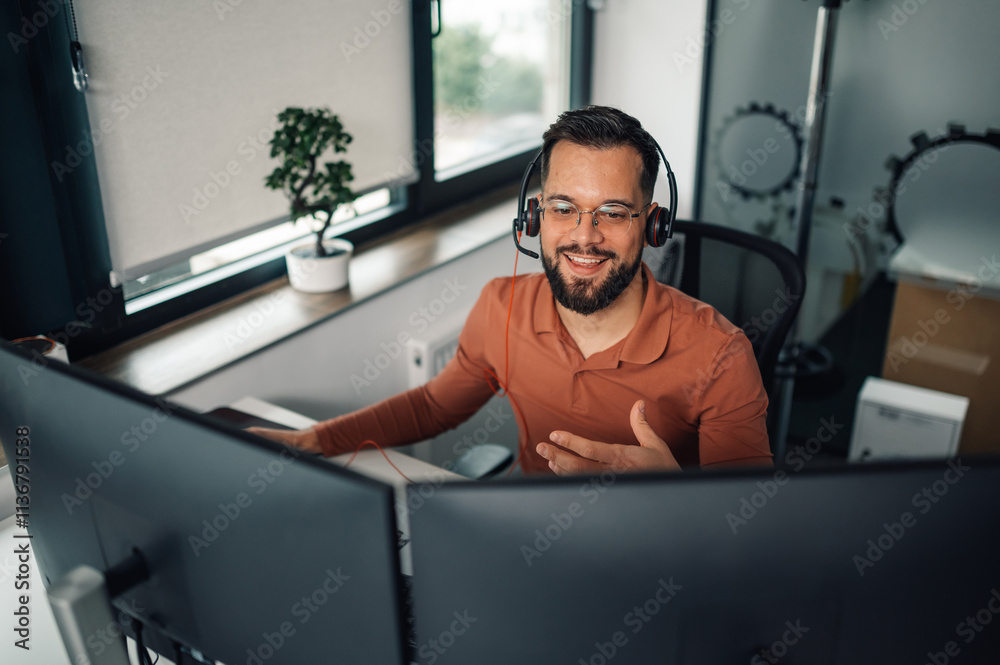 Smiling businessman having video call and working from home office using dual monitor setup ...