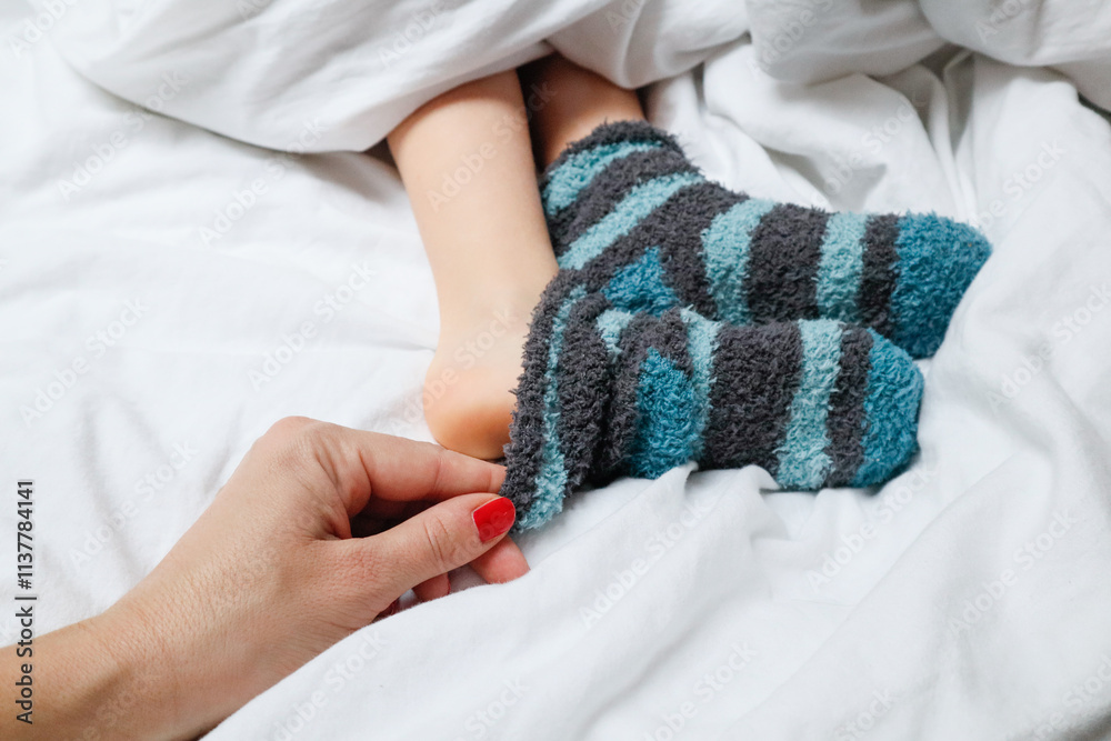 Mom pulling off baby’s sock while child lies in bed Stock Photo | Adobe ...