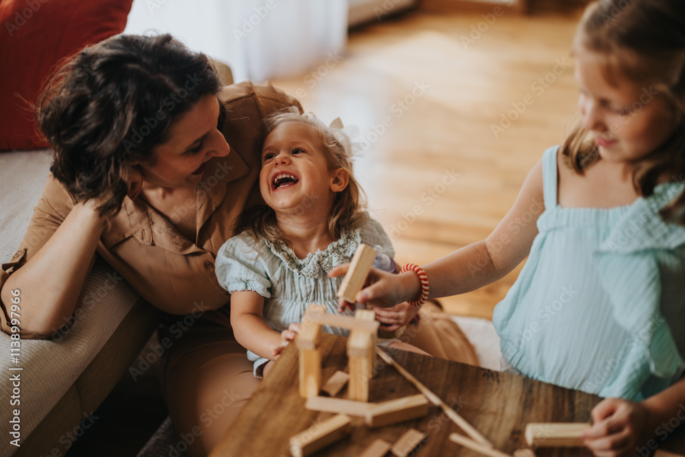 Joyful mother spending quality time with her daughters as they play with wooden blocks ...