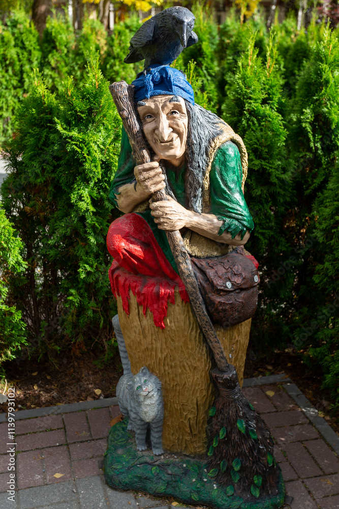 Wooden figure of Baba Yaga in the park against the background of trees ...
