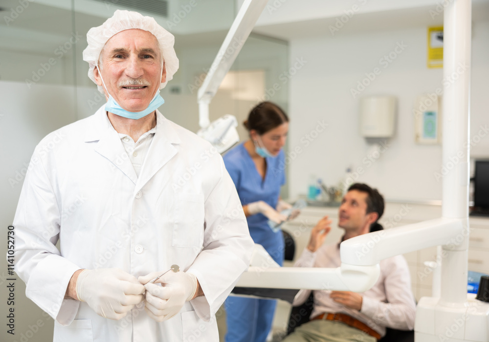 Mature male doctor is standing in dental office, clinic employee in ...