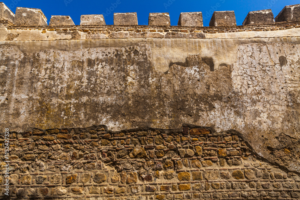weathered stone wall with a crenellated top, revealing layers of ...