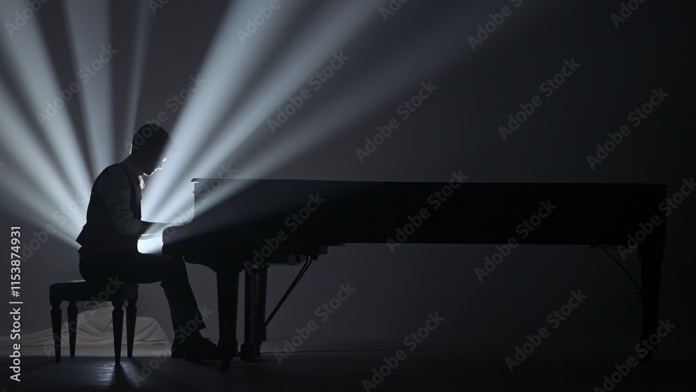 Pianist sitting and playing on the black grand piano on dark concert ...