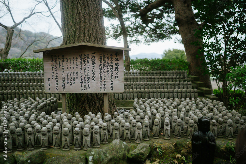 Hundreds of small, weathered stone Jizo statues line the base of a tree ...