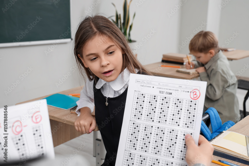 Cute schoolgirl receiving answer sheet with B grade from teacher in ...