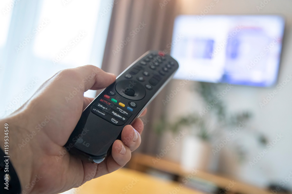A close-up shot of a hand holding an LG remote control, with focus on ...