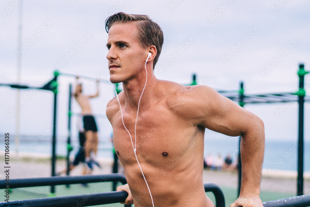 Caucasian strong athlete doing exercises on outdoors bars listening ...