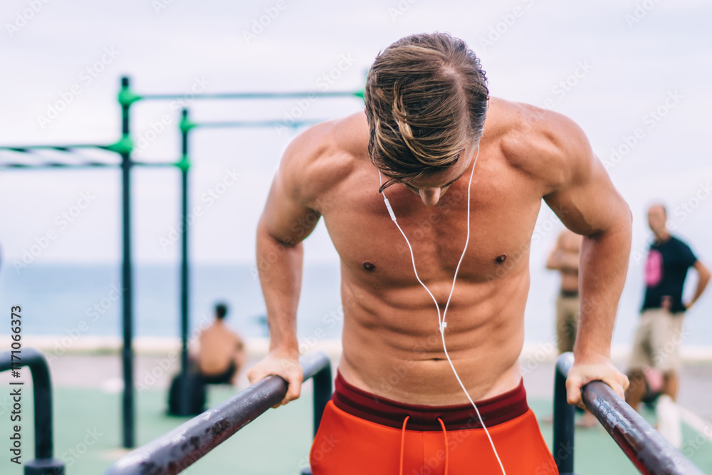 Caucasian strong athlete doing exercises on outdoors bars listening ...
