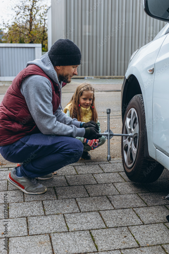 A little girl assists her father in changing the car tires,creating ...