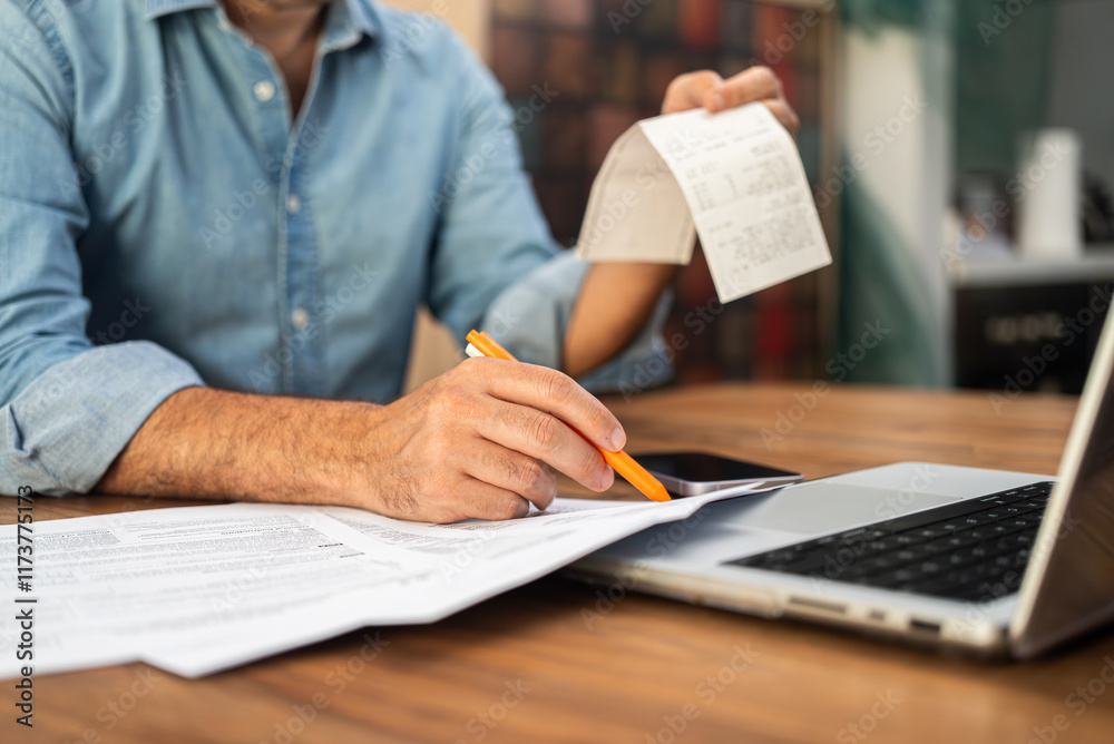 Man filling out tax forms at home using a laptop and holding receipts ...