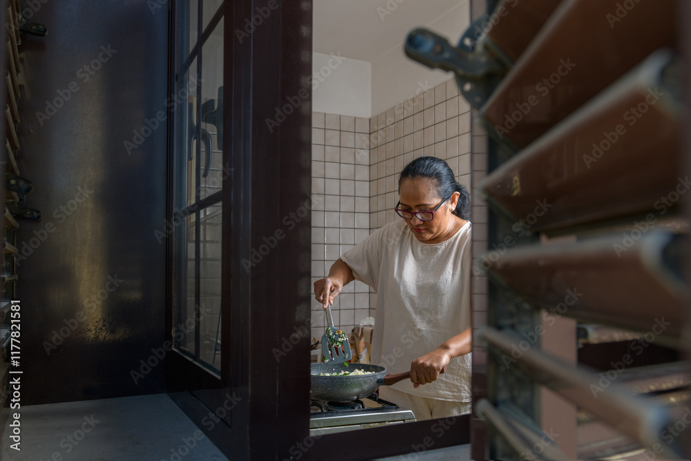 Indonesian woman cooking fried rice in the kitchen, window framing ...
