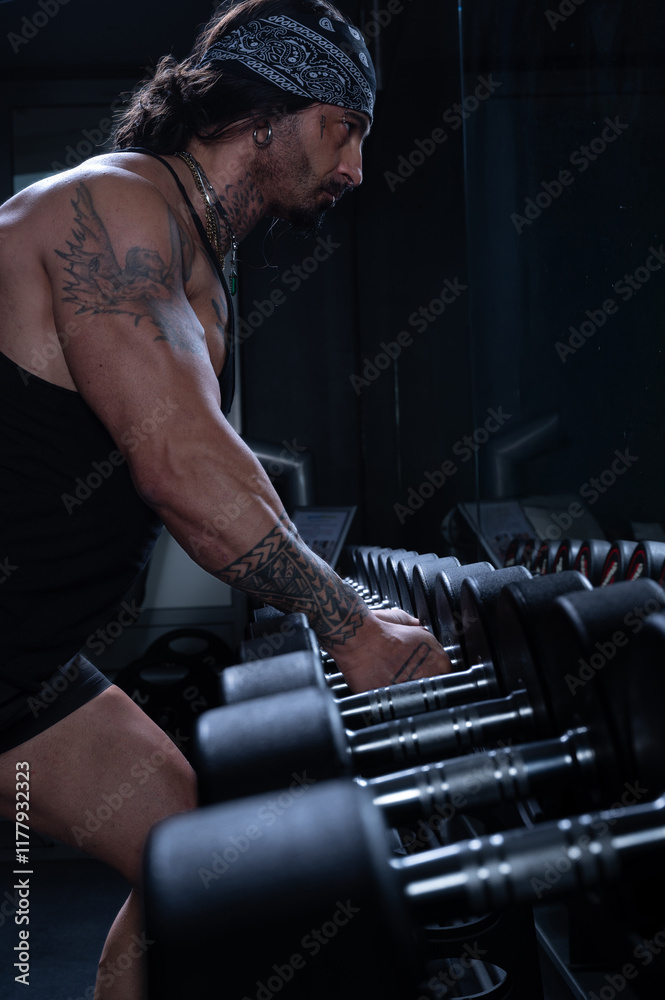 Tattooed male bodybuilder dumbbell rack perspective dark gym ...