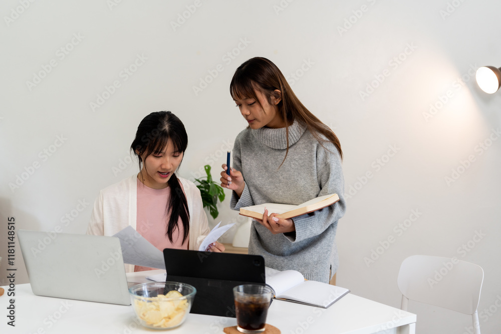 Female higher education student using laptop and studying book in home ...